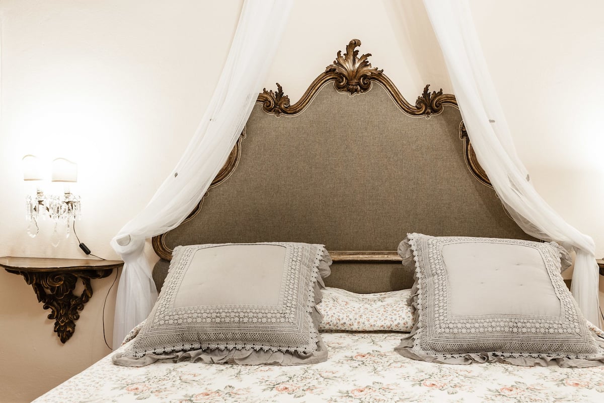 Uma cama com dossel, duas mesas de cabeceira com luminárias e um edredom estampado com flores.
