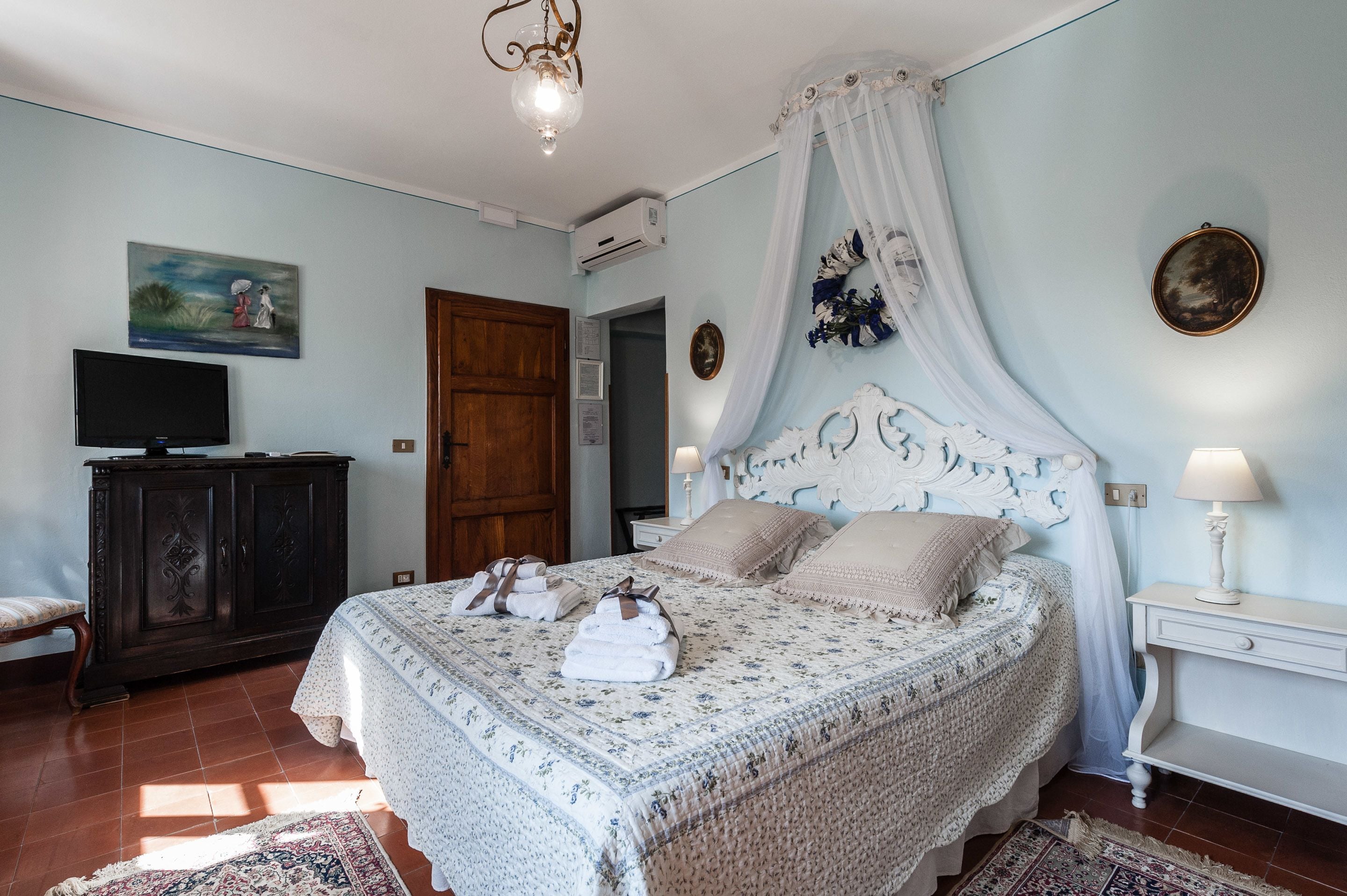 Um quarto com cama, mesa de cabeceira, televisão e guarda-roupa.