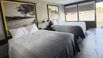 Quarto de hotel com duas camas, janela com vista para um estacionamento e quadros nas paredes.