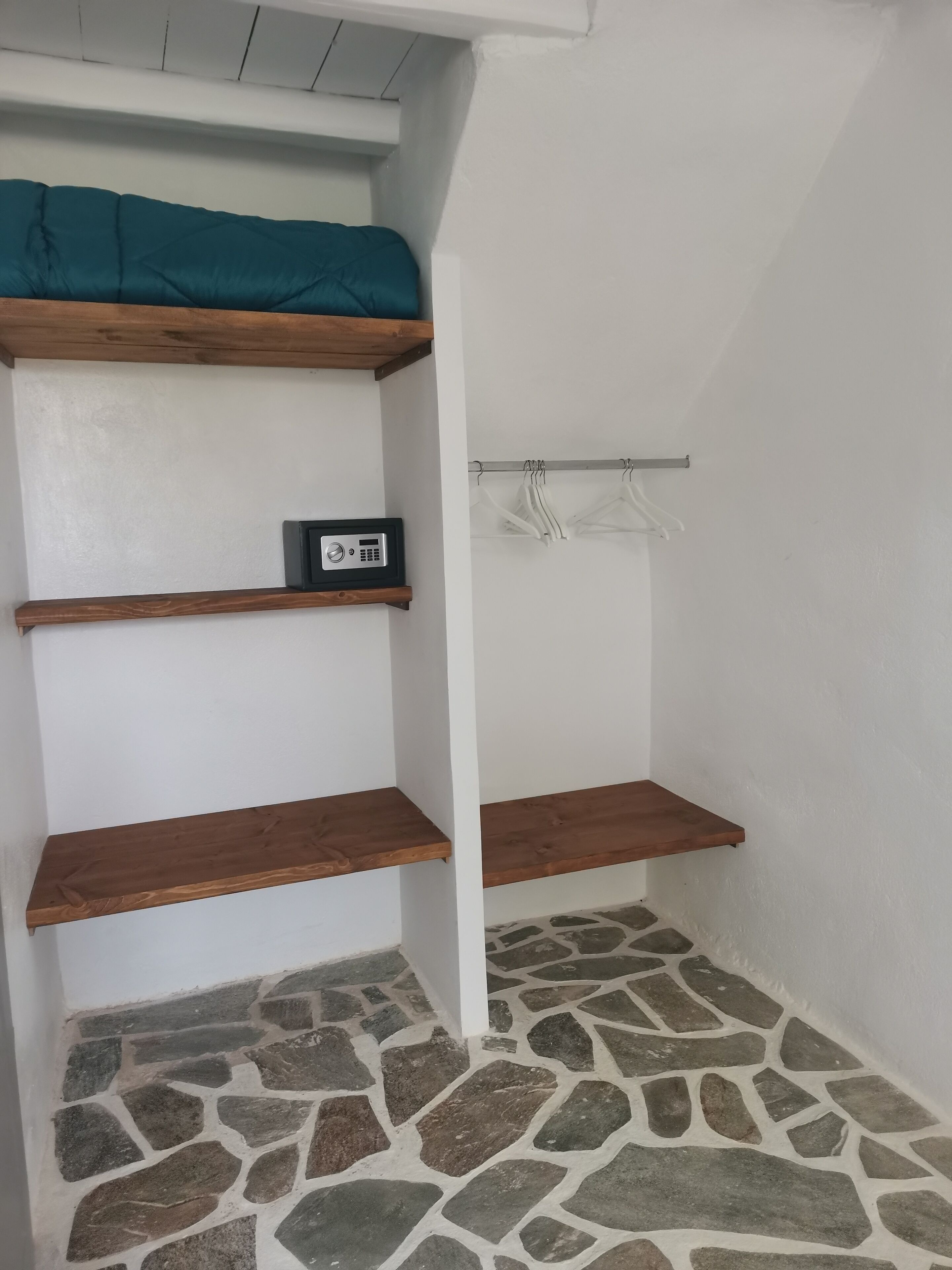 Quarto de canto com piso de pedra, paredes brancas e prateleiras de madeira.