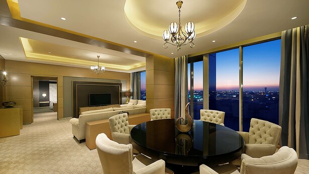 Quarto de hotel moderno com mesa de jantar redonda, assentos confortáveis, televisão de tela plana e vista para a cidade.