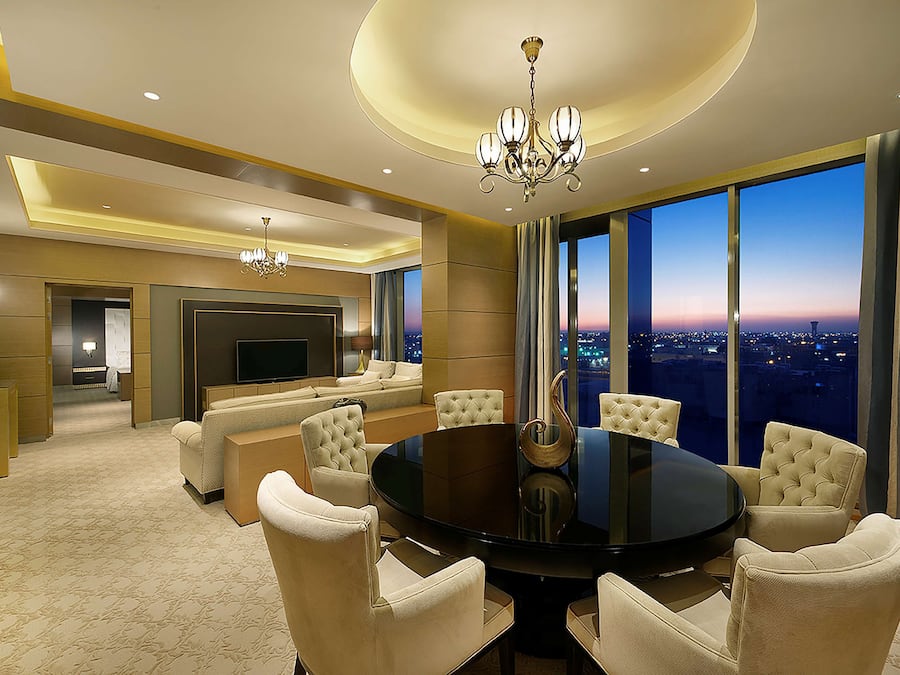 Quarto de hotel moderno com mesa de jantar redonda, assentos confortáveis, televisão de tela plana e vista para a cidade.