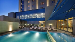 Um hotel moderno com piscina, espreguiçadeiras e fachada de vidro.
