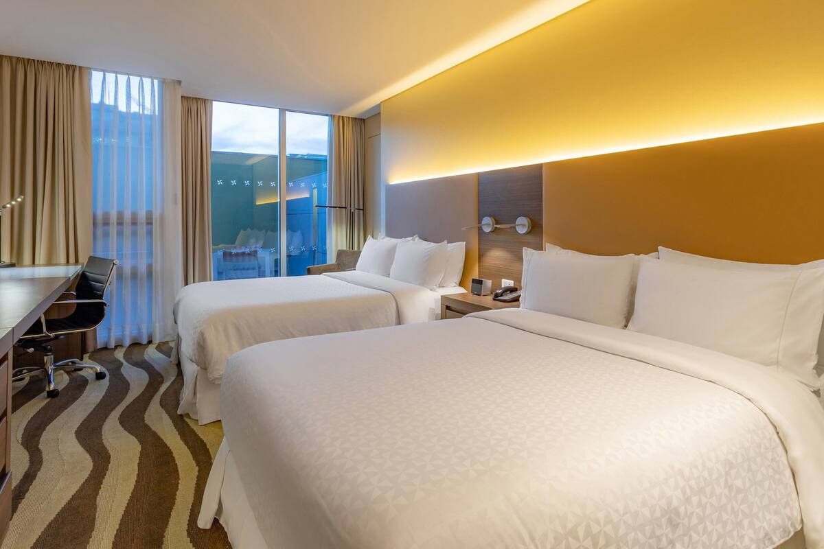 Quarto de hotel com duas camas, uma escrivaninha e uma cadeira.