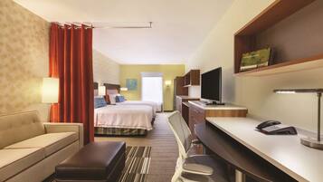 Quarto de hotel com cama, escrivaninha, cadeira, sofá, televisão e abajur.