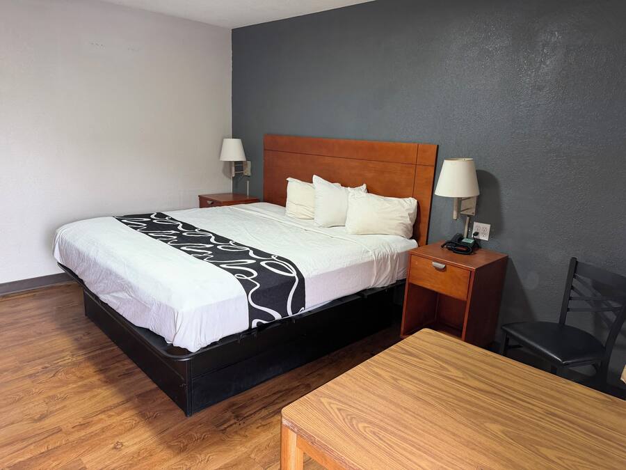 Quarto de hotel com cama, mesas de cabeceira, escrivaninha e uma cadeira.