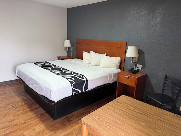 Quarto de hotel com cama, mesas de cabeceira, escrivaninha e uma cadeira.