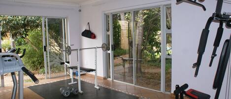 Uma academia em casa com equipamentos de exercício, uma porta de correr com vidro que dá para um jardim e um tapete no chão.