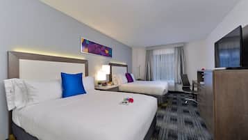 Quarto de hotel com duas camas, uma escrivaninha, televisão e um quadro na parede.