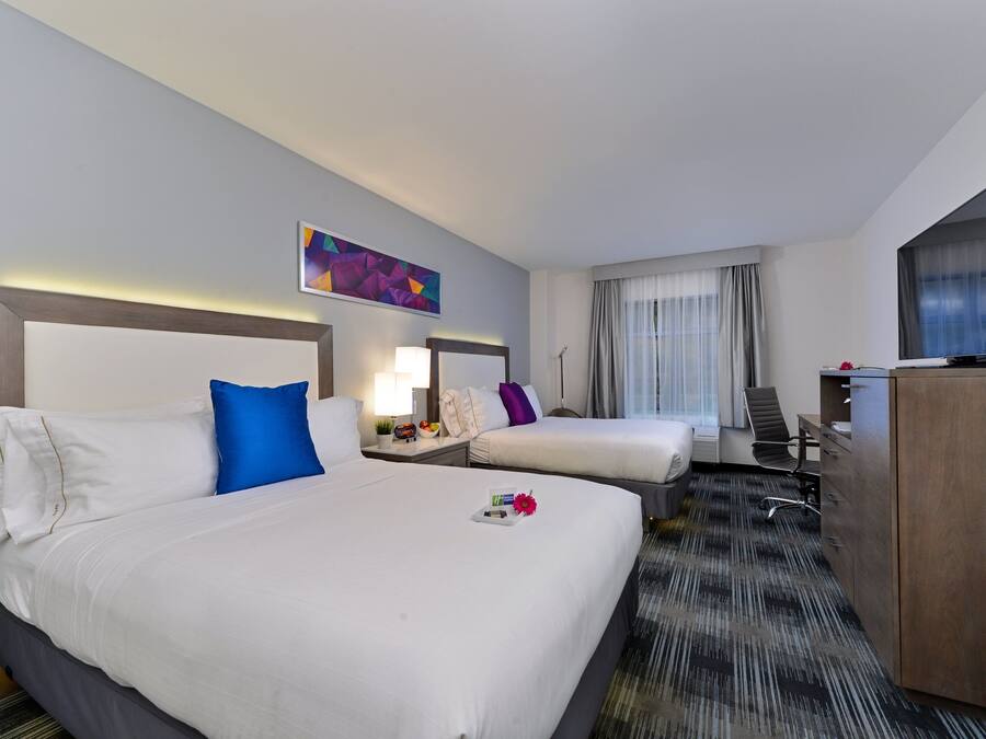 Quarto de hotel com duas camas, uma escrivaninha, televisão e um quadro na parede.