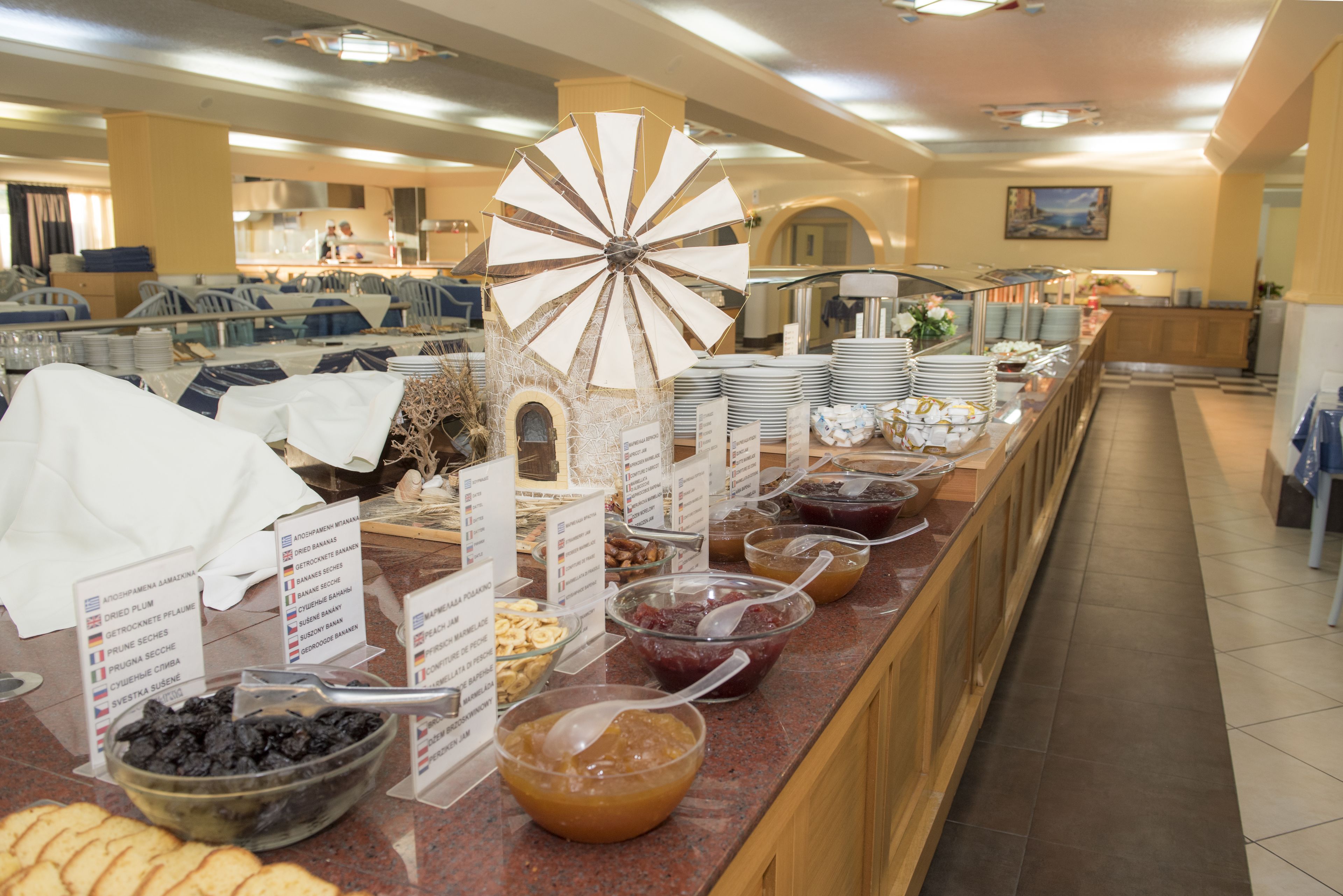 Uma área de buffet com diversas opções de comida, incluindo tigelas de frutas e outros pratos, dispostos em um balcão com placas indicativas.