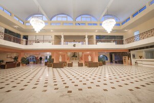 Um hall espaçoso com teto alto, grandes lustres, área de recepção e uma estátua central.
