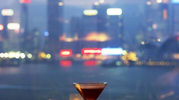 Uma mesa com um copo de martini, uma vela e pratos de comida, com um horizonte urbano ao fundo.