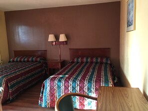 Quarto de hotel com duas camas, uma mesa de cabeceira, duas luminárias fixadas na parede e uma cadeira de madeira.