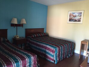 Quarto com duas camas, uma mesa de cabeceira com abajur, uma pequena mesa e um quadro pendurado na parede.