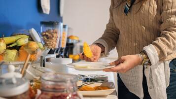 Uma mesa de buffet com diversos alimentos e uma pessoa servindo fatias de laranja.