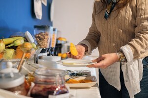 Uma mesa de buffet com diversos alimentos e uma pessoa servindo fatias de laranja.