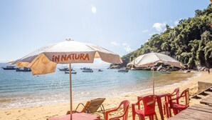 Um restaurante à beira-mar com mesas ao ar livre e guarda-sóis com a inscrição "in Natura".