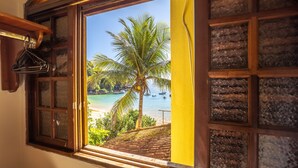 Uma janela com vista para uma praia, uma palmeira e barcos.