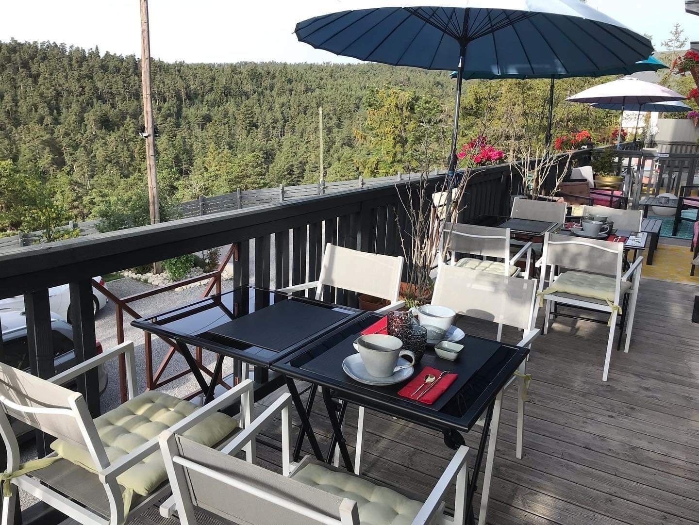 Um terraço ao ar livre com mesas, cadeiras, guarda-sóis e vista para uma área arborizada.