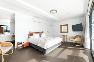 Quarto de hotel moderno com uma cama grande, mesas de cabeceira, escrivaninha, uma cadeira e uma televisão.