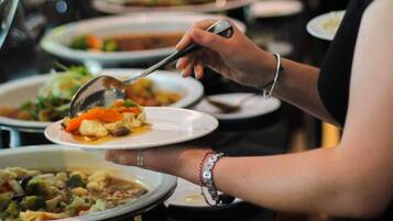 Uma mesa de buffet com diversos pratos e alguém se servindo.