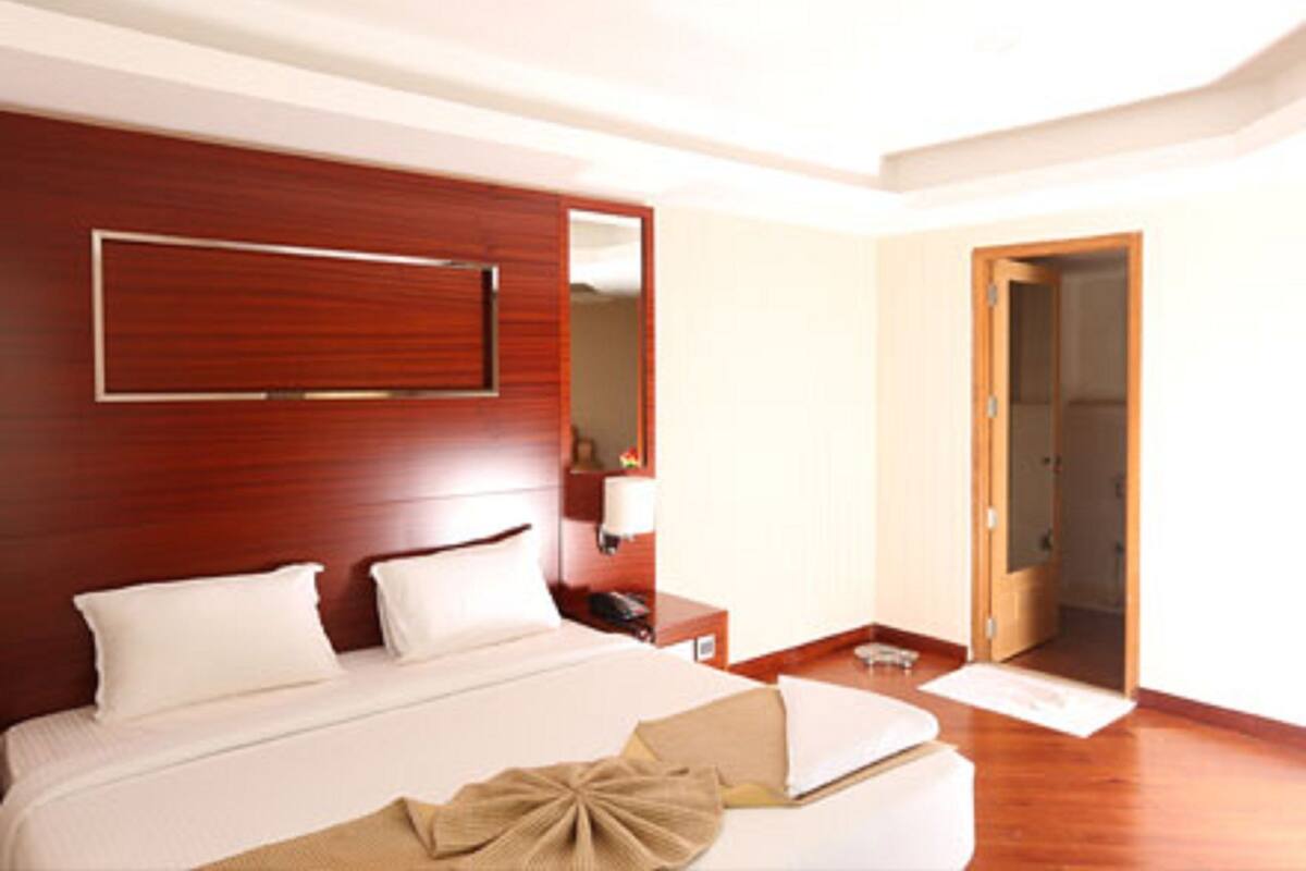 Quarto de hotel com uma cama grande, cabeceira de madeira, mesa de cabeceira com abajur e porta que dá para outro cômodo.