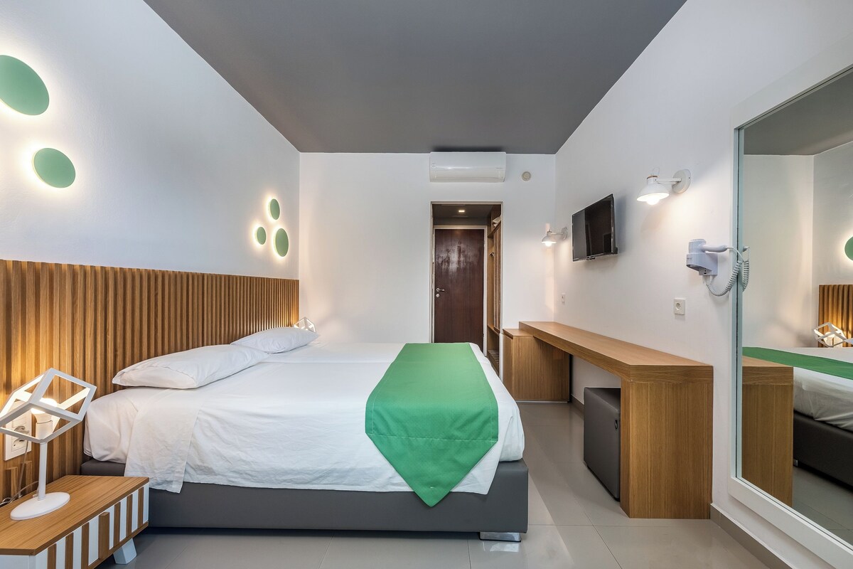 Quarto de hotel moderno com cama, mesa de cabeceira e área de trabalho.