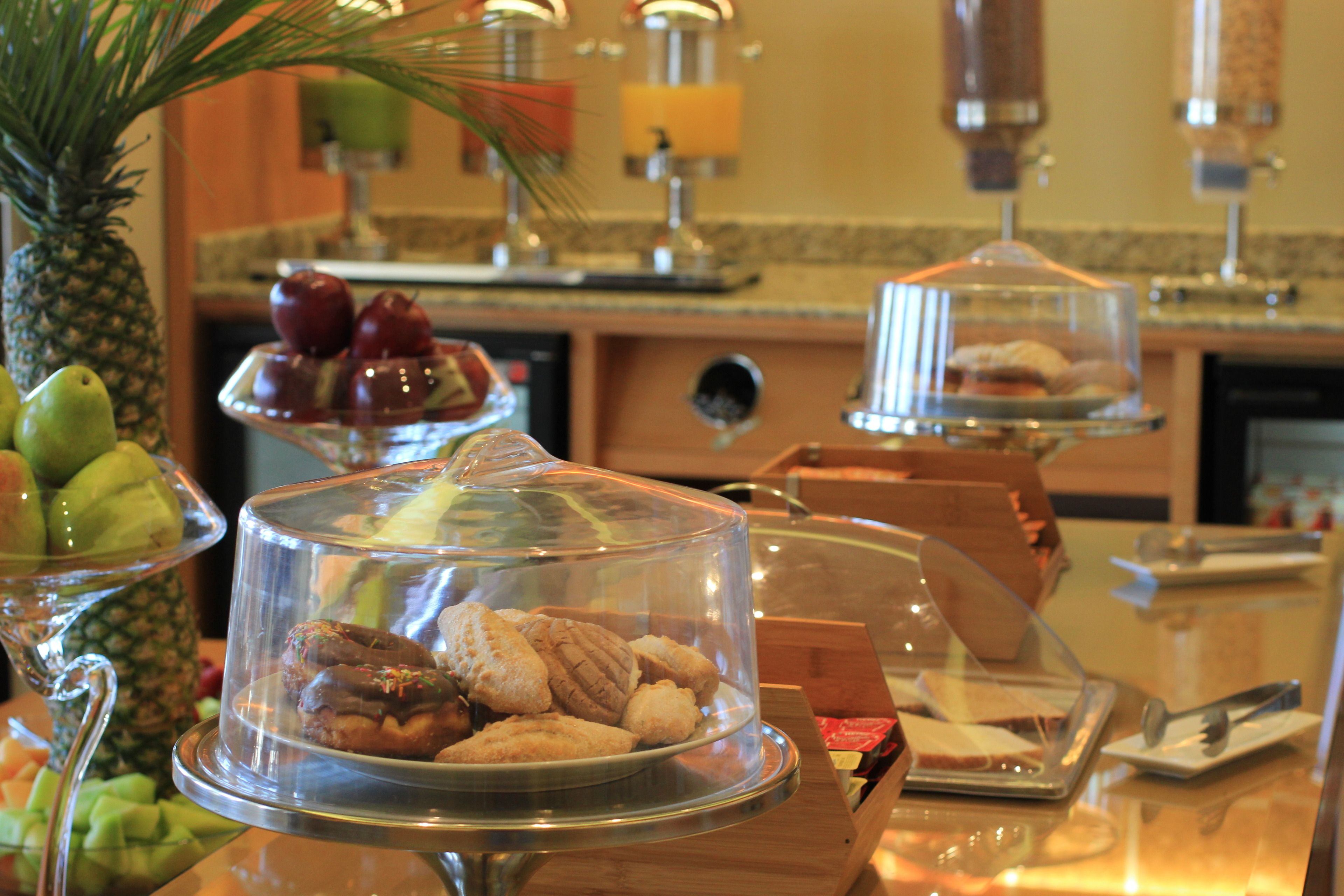 Buffet com diversos alimentos sob proteção de vidro, incluindo doces, frutas e uma abacaxi.