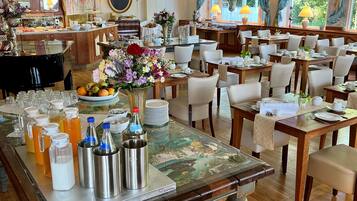 Uma sala de jantar com várias mesas preparadas para o café da manhã, um buffet e uma variedade de bebidas e pratos.