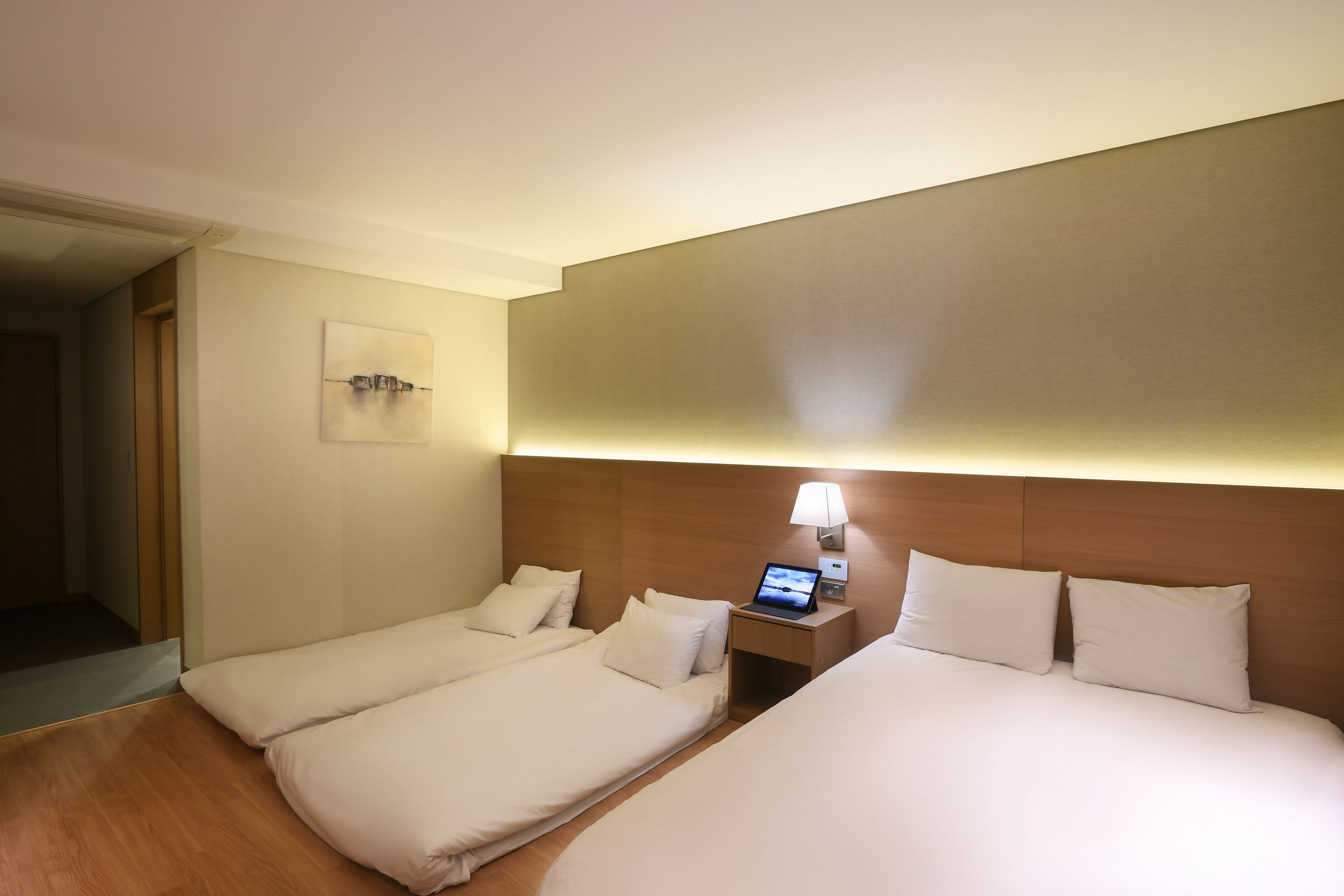 Quarto de hotel com duas camas, uma mesa de cabeceira e uma luminária, e um laptop.