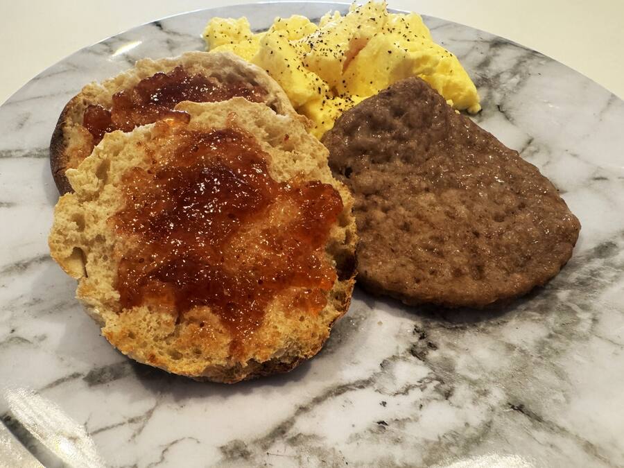 Um prato com três tipos diferentes de comida: um biscoito com geleia, purê de batatas e um hambúrguer.