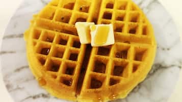 Uma waffle com calda e um pouco de manteiga sobre um prato de mármore.
