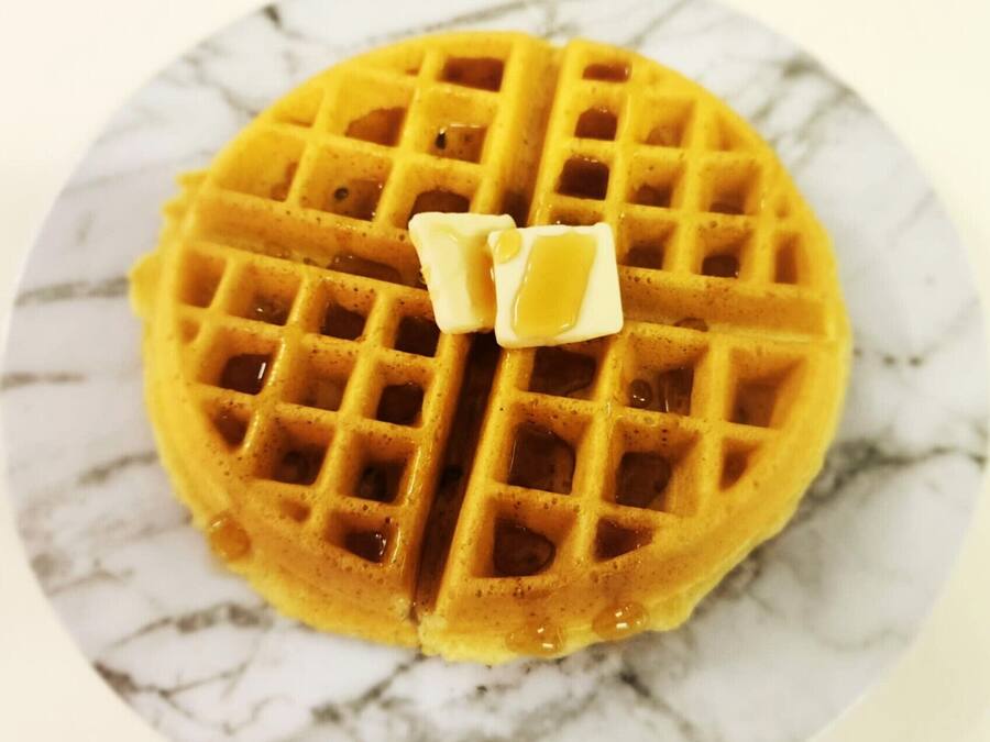 Uma waffle com calda e um pouco de manteiga sobre um prato de mármore.
