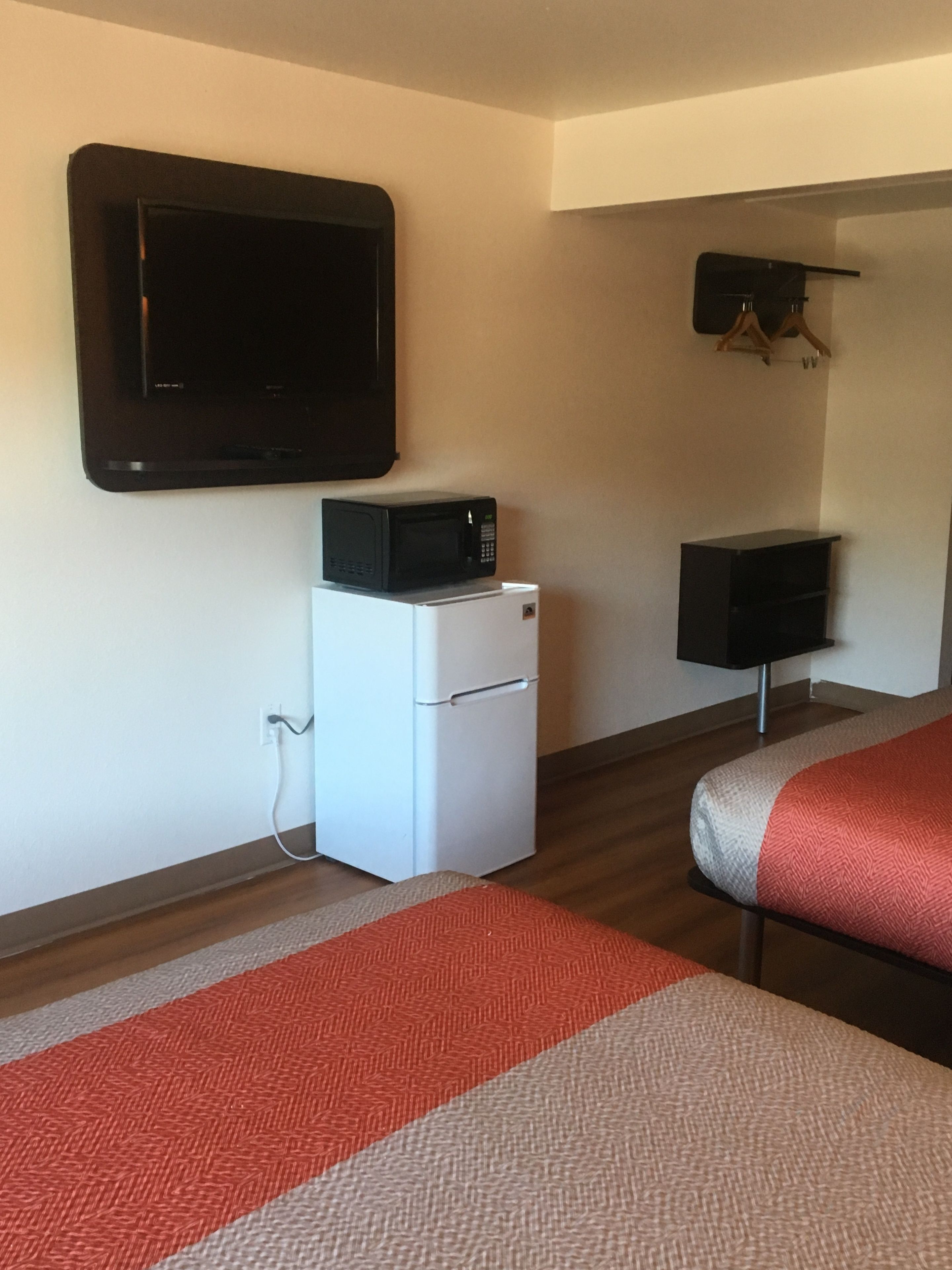 Quarto de hotel compacto com uma cama, um frigorífico branco, micro-ondas, televisão e um pequeno armário preto.