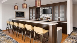 Uma área de bar com um balcão comprido, banquetas acolchoadas, uma TV montada e um menu em lousa.