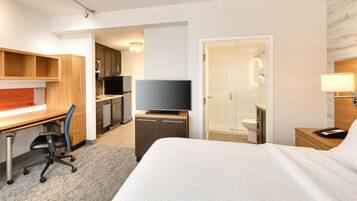 Quarto de hotel com cama, escrivaninha, televisão, cozinha compacta e banheiro.