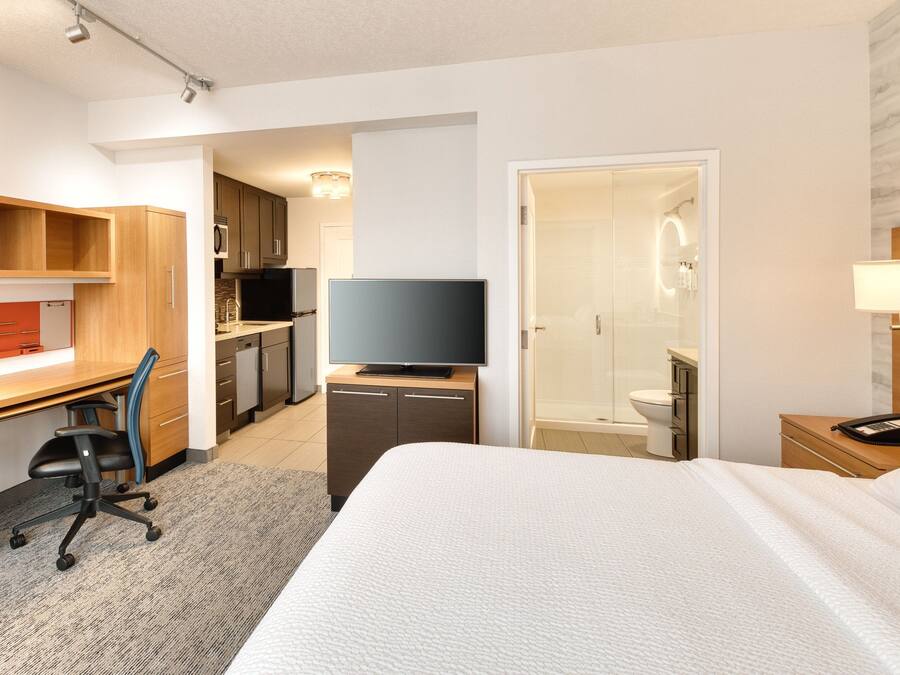 Quarto de hotel com cama, escrivaninha, televisão, cozinha compacta e banheiro.
