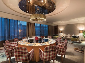 Uma mesa de jantar redonda com cadeiras xadrez, um lustre e vista para o exterior através de amplas janelas.