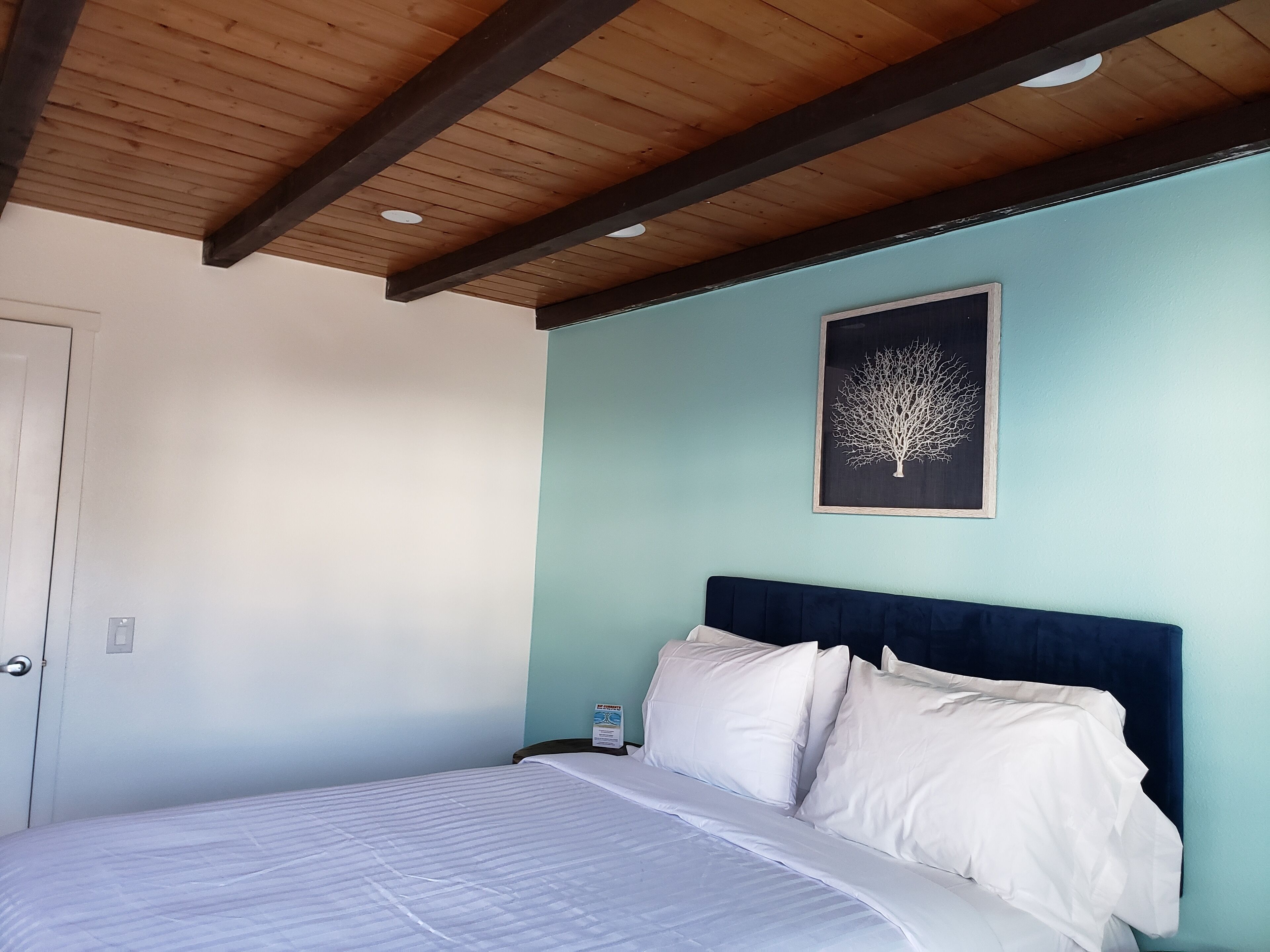 Quarto com cama, cabeceira, uma obra de arte na parede e uma porta.