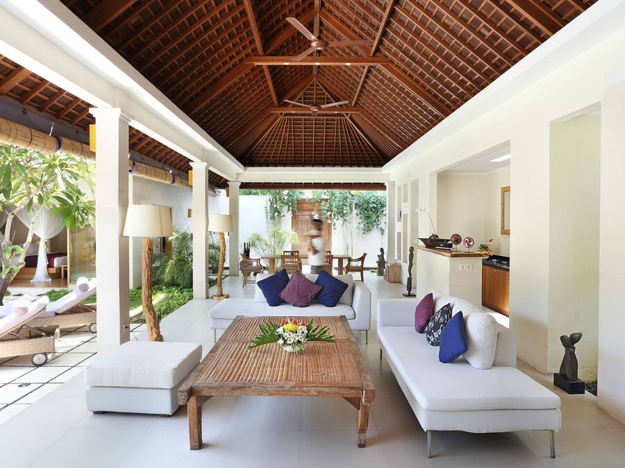 Um espaço amplo e interno com teto alto, teto de madeira, sofá branco e mesa de centro de madeira, além de vista para o jardim externo.