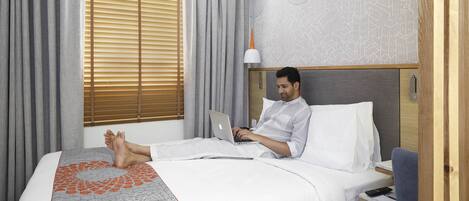 Quarto de hotel com cama, um laptop, mesa de cabeceira e janela com persianas.