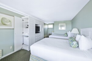 Quarto de hotel com uma cama grande, um guarda-roupa com televisão e uma mesa de cabeceira com abajur.