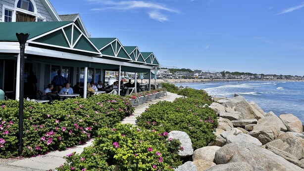 Um restaurante à beira-mar com área externa, vista para o oceano e um litoral rochoso.