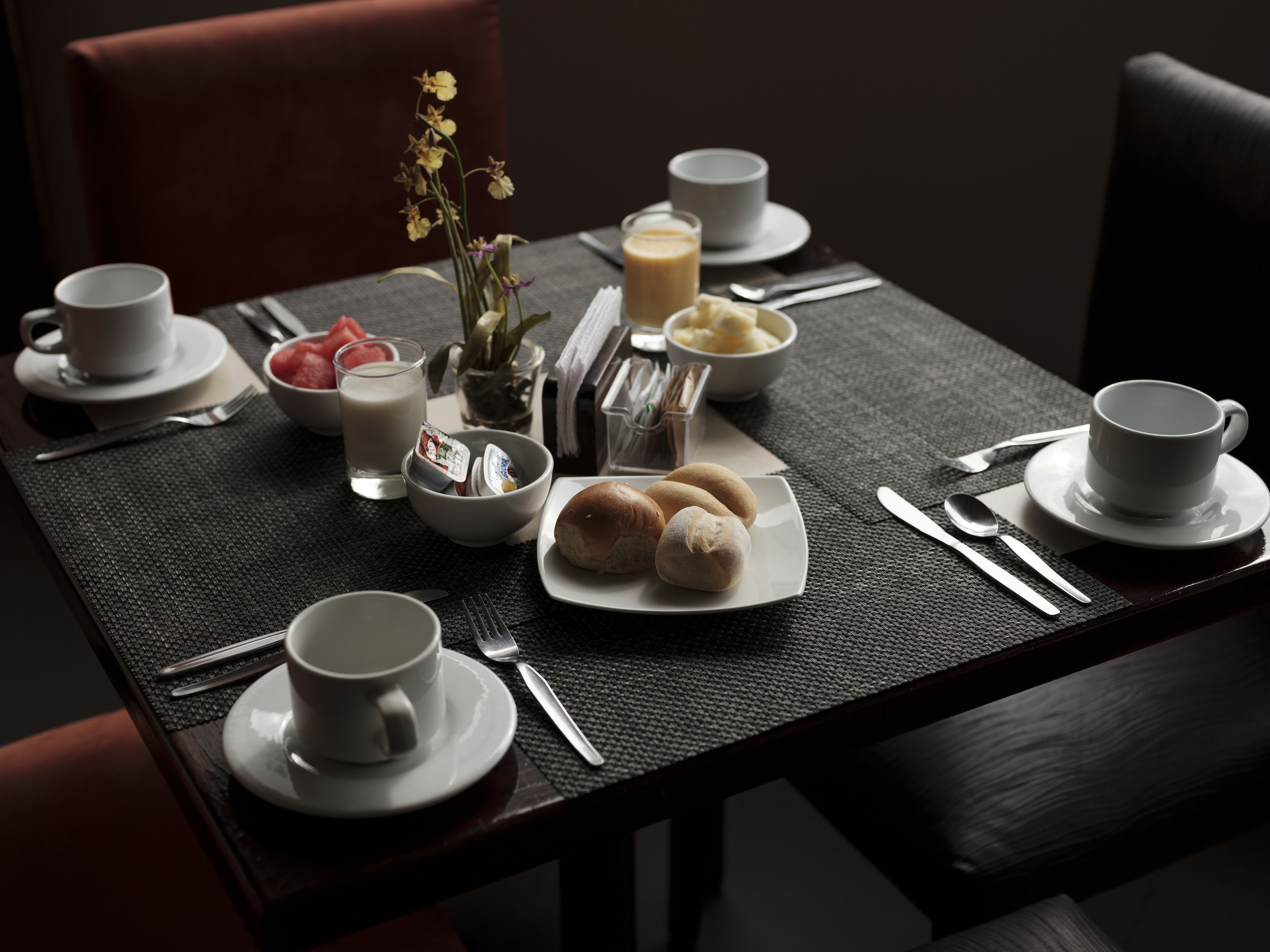 Uma mesa posta para dois, com pratos de pastelaria, tigelas de fruta e xícaras de café.