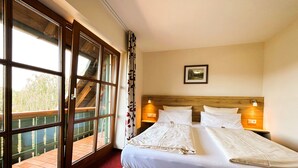 Quarto de hotel com uma cama grande, duas mesas de cabeceira com luminárias, uma janela com vista para uma varanda e um quadro na parede.