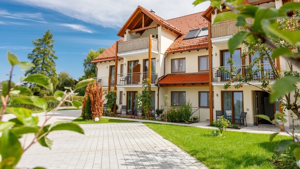 Um edifício residencial de vários andares com varandas, entrada com calçada e gramado bem cuidado.