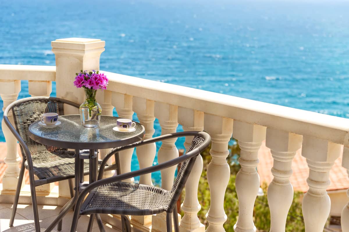 Uma varanda com mesa redonda e duas cadeiras de vime, com vista para um corpo de água.