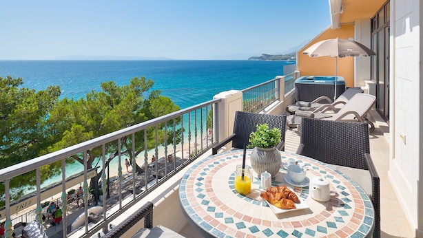 Varanda com vista para o mar, uma mesa redonda com um croissant e uma bebida, e uma banheira de hidromassagem.