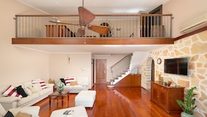 Uma sala de estar ampla com escada de madeira, ventilador de teto e parede de pedra.